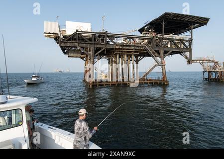 An angler fishes for baitfish while surrounded by offshore oil ...