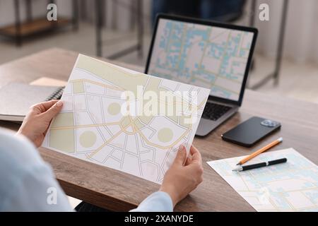 Cartographer working with cadastral maps at wooden table in office ...