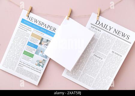 Newspapers and blank sheet of paper hanging on rope against pink ...