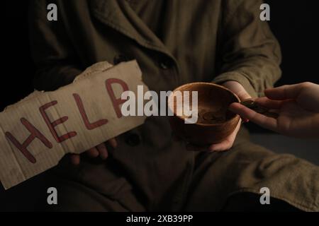 Woman giving coins to homeless with help sign, closeup. Charity and ...
