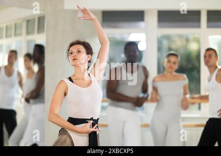 Female ballet instructor demonstrating movements to group of dancers ...