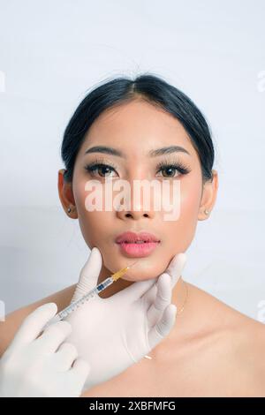 Young woman receiving filler injection in face against pink background ...