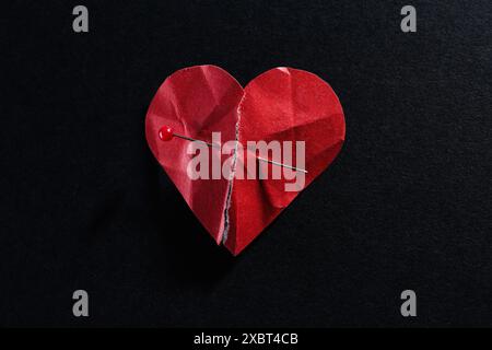Halves of torn paper heart connected by sewing pin on black background ...