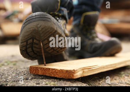 Careless worker stepping on nail in wooden plank outdoors, closeup ...