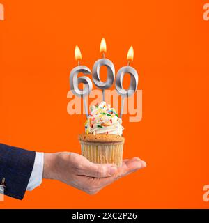 Hand holding a cupcake with the number 600 candle - Birthday on blue ...