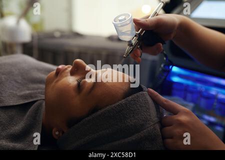 Spraying hydrating emulsion on face of woman after beauty treatment ...