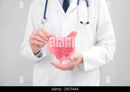 Doctor with paper intestine cutout on light grey background, closeup ...