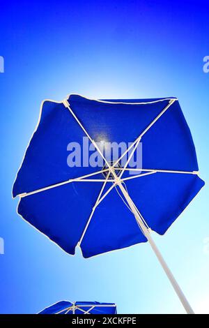The sun shining through a blue parasol against blue sky, Greek Island ...