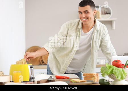 Young man making crispy toasts for sandwiches in kitchen Stock Photo ...