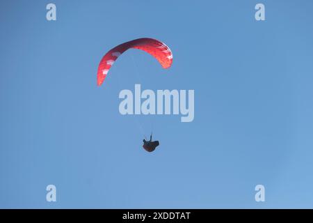 A single paraglider with a red and white canopy, against a clear, blue ...
