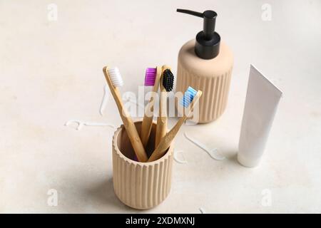 Cup with toothbrushes, tube of toothpaste and soap dispenser on beige ...