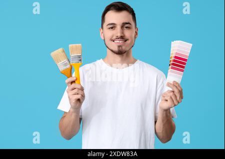 Young man with color palettes and brushes on pink background with space ...