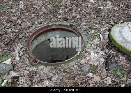 an open manhole in the woods, the ground is strewn with old autumn ...