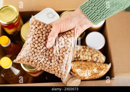 Plastic container with chickpeas in female hand on emergency food box ...