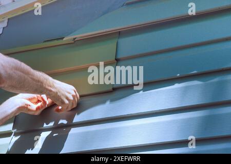 Workers install vinyl plastic siding panels on facade of new home ...