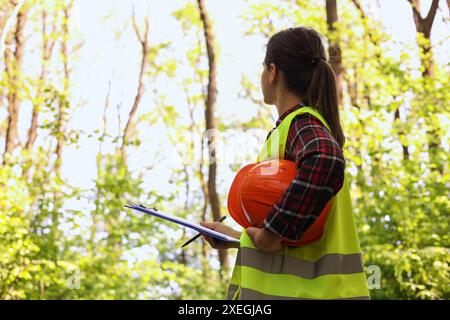 Forester in hard hat with clipboard examining plants in forest Stock ...