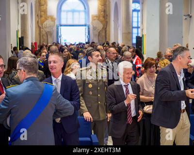 A diverse crowd of people gathered indoors, looking upwards with varied ...