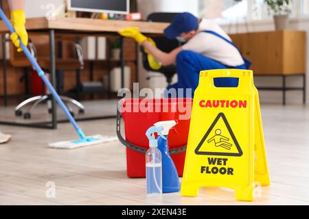 Caution sign with bottles of detergent and bucket on floor in office ...