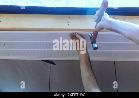 An employee installs soffit on roof corner of house constructed from ...
