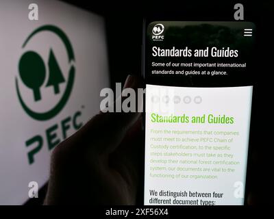 Person holding cellphone with logo of Programme for the Endorsement of ...