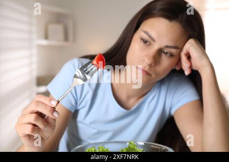 Eating disorder. Sad woman holding fork with cucumber over bowl at ...