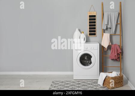 Washing machine, detergents, ladder, basket and laundry near grey wall ...