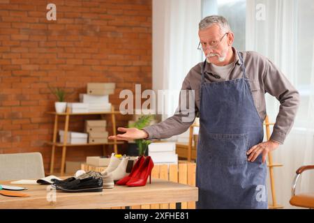 An elderly shoemaker showing handmade male shoes and belt in a workshop ...