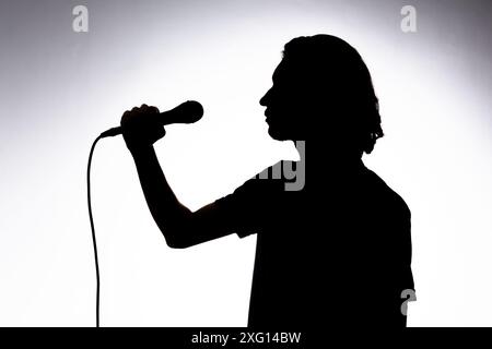 Silhouette of young singer holding wired microphone. Isolated on white ...