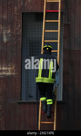 Firefighter in uniform with portective helmet climbing ladder during ...