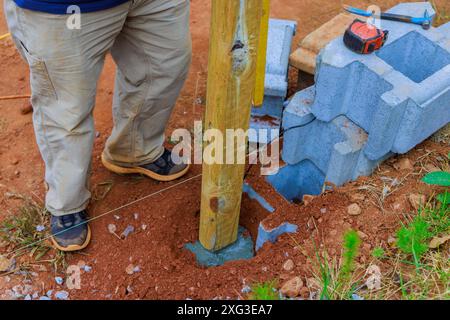Pouring concrete over newly installed timber fencing wooden fence posts ...
