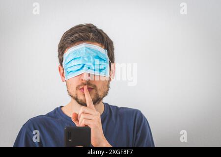 Young angry man with face mask over the eyes is doing a psst! gesture ...