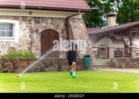 Young white boy running under the water from the sprinkler in the ...