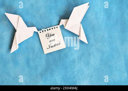 Two white dove carrying white card with you are invited message in blue ...