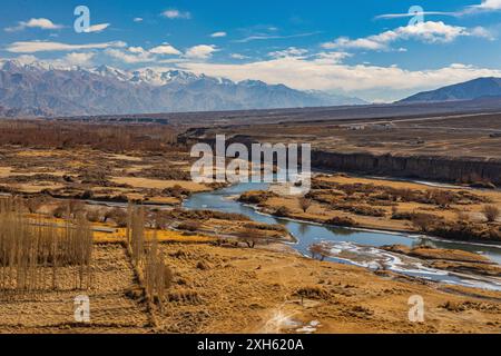 Indus river flowing through dry winter grass with snow-clad mountains ...