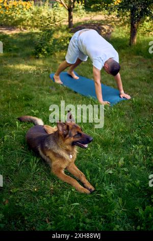 a man does somatic exercises with his dog in the garden in the morning ...