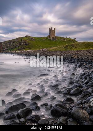 The ruins of Dunstanburgh castle ubove the black rocks of Rumble Churn ...