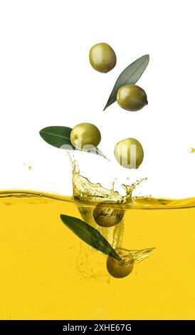 Green olives and leaves falling into cooking oil on white background ...