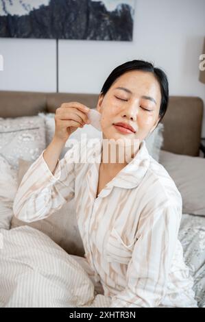 Asian woman massaging face with jade rollers isolated on pink Stock Photo - Alamy