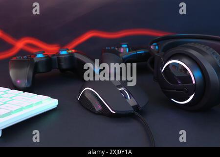 Computer mouse, headset, RGB keyboard and game controllers in neon lights on dark background ...