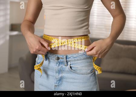 Underweight young woman measuring her waist with a tape measure with ...