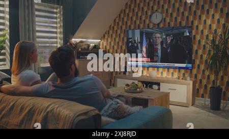 Adult couple talks and watches news broadcast report about US Election Day on the big TV screen ...