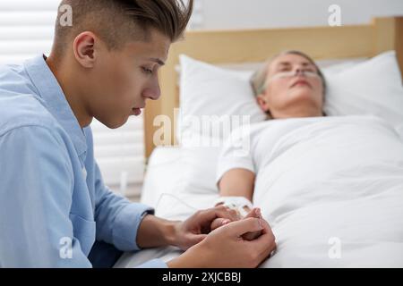 Coma patient. Sad young man near his unconscious mother talking with ...