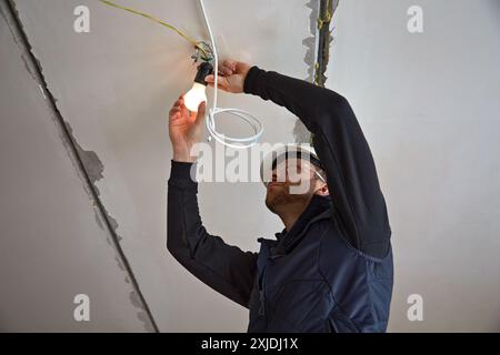 Portrait of male electrician, focused on wiring a temporary light bulb ...