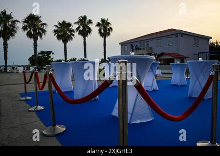 Vip area is set up outside for an event with white cocktail tables, red ...