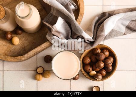 Glass and bottles of fresh macadamia milk on white tile background ...