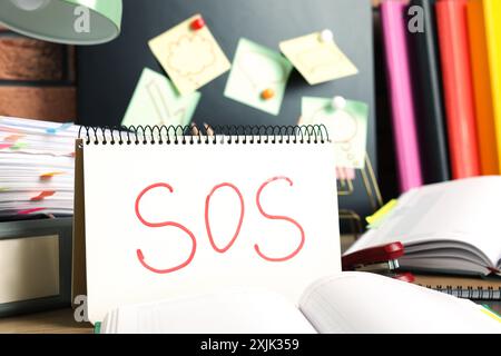 Notebook with word SOS and stationery on wooden table at workplace ...