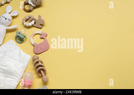 Colorful rattles, diapers, bottle and pacifiers on yellow background ...