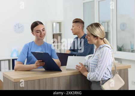 Professional receptionist working with patients at wooden desk in ...