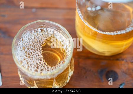 A glass mug containing an amber liquid sits on a dark surface ...