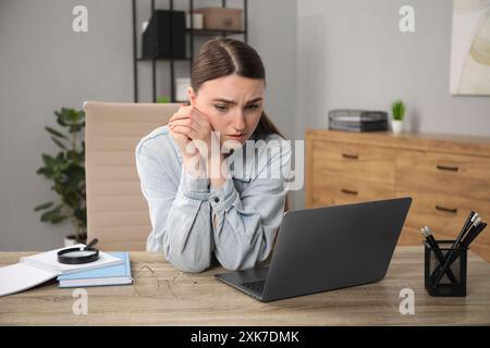 Embarrassed woman at wooden table with laptop in office Stock Photo - Alamy